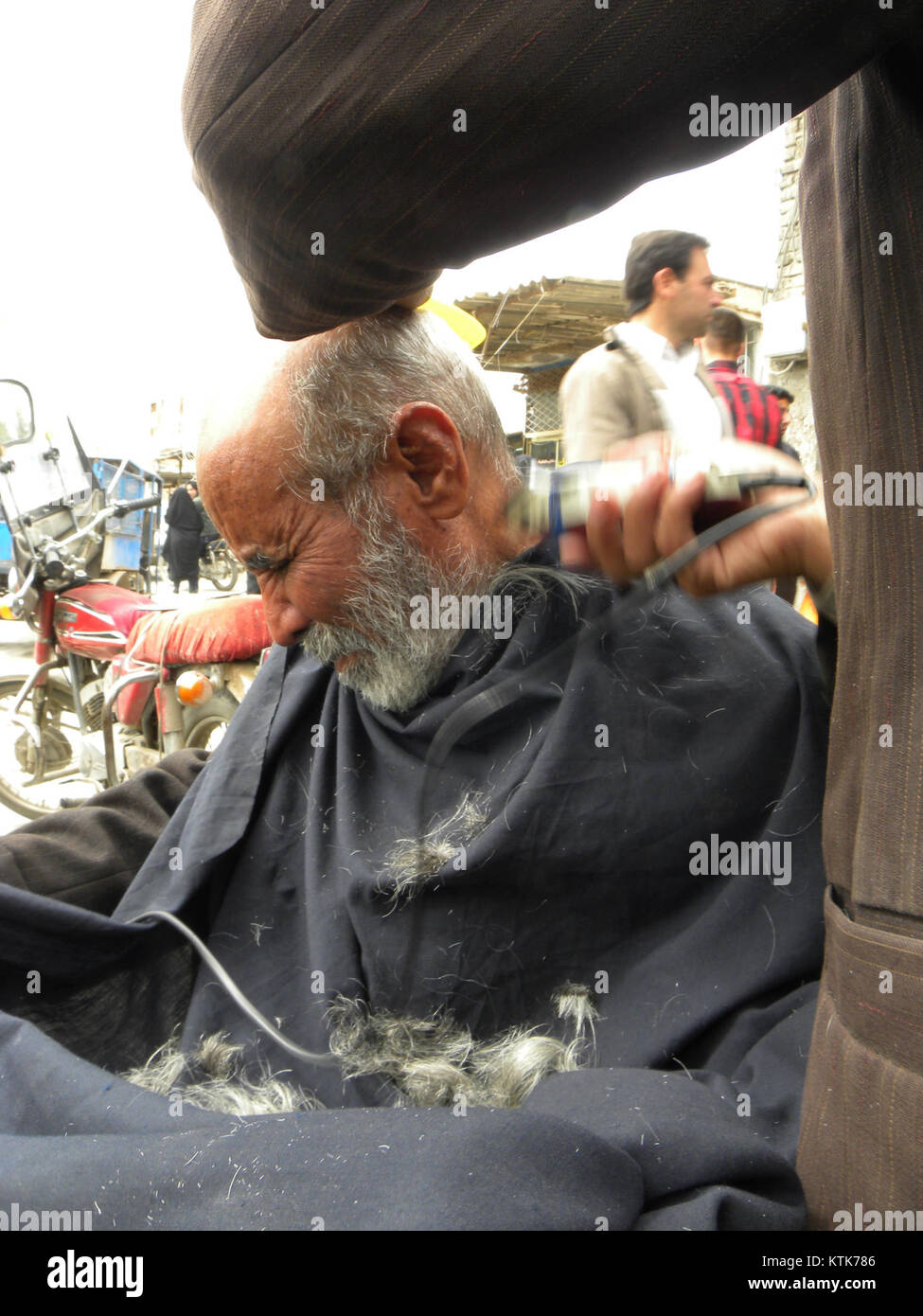 A street scene in Nishapur shows a barber working on the sidewalk ...