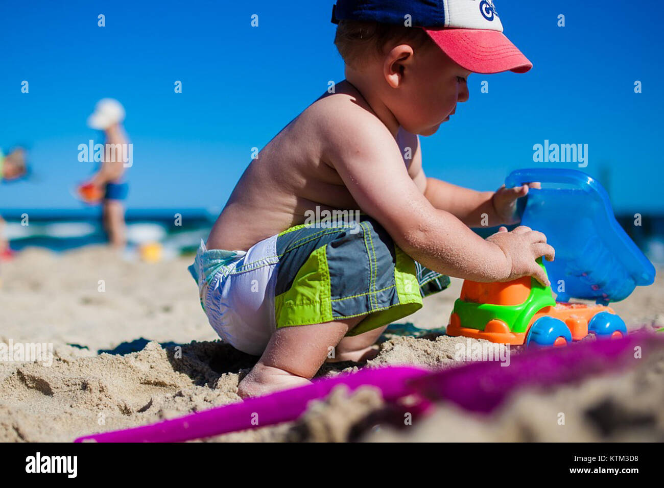 A baby playing on the beach enjoys the sand and surf in a typical ...