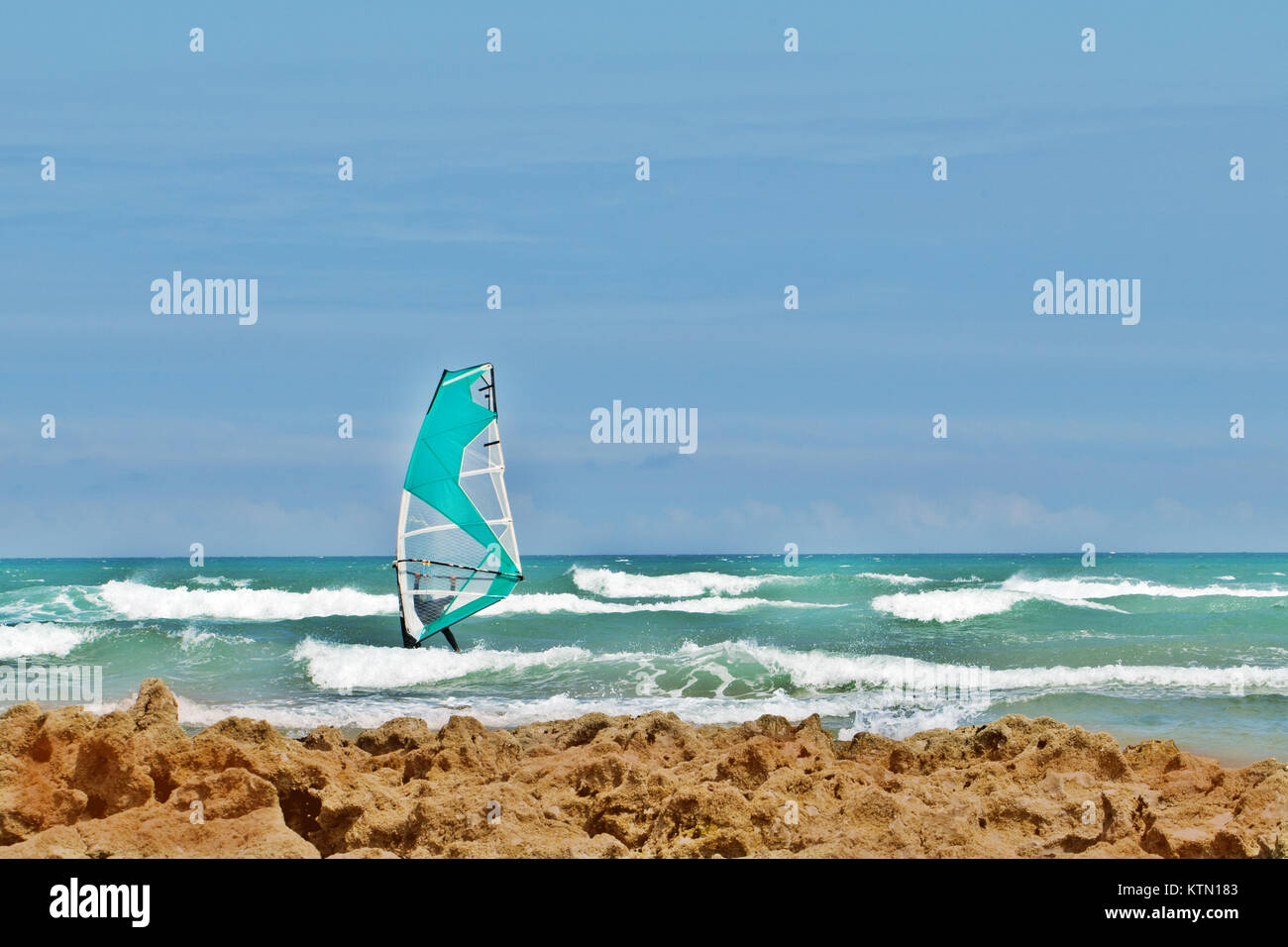 The windsurfer with a sail and coast among waves. Blue sky, sunny ...