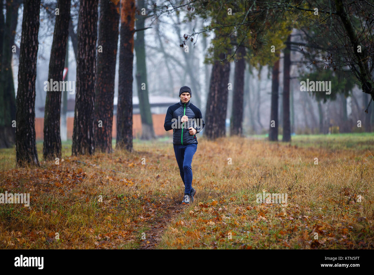 Young man jogging in fall park. Trail running in cold and misty weather ...