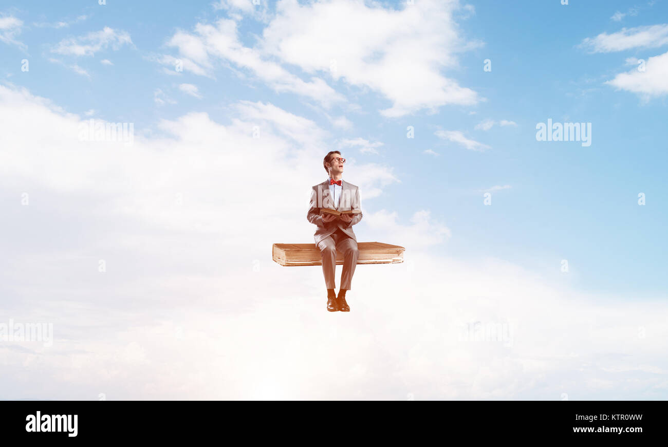 Young businessman or student floating in blue sky and studying the ...