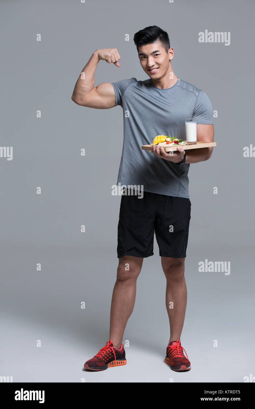 Young male athlete flexing muscles while holding vegetable salad and ...