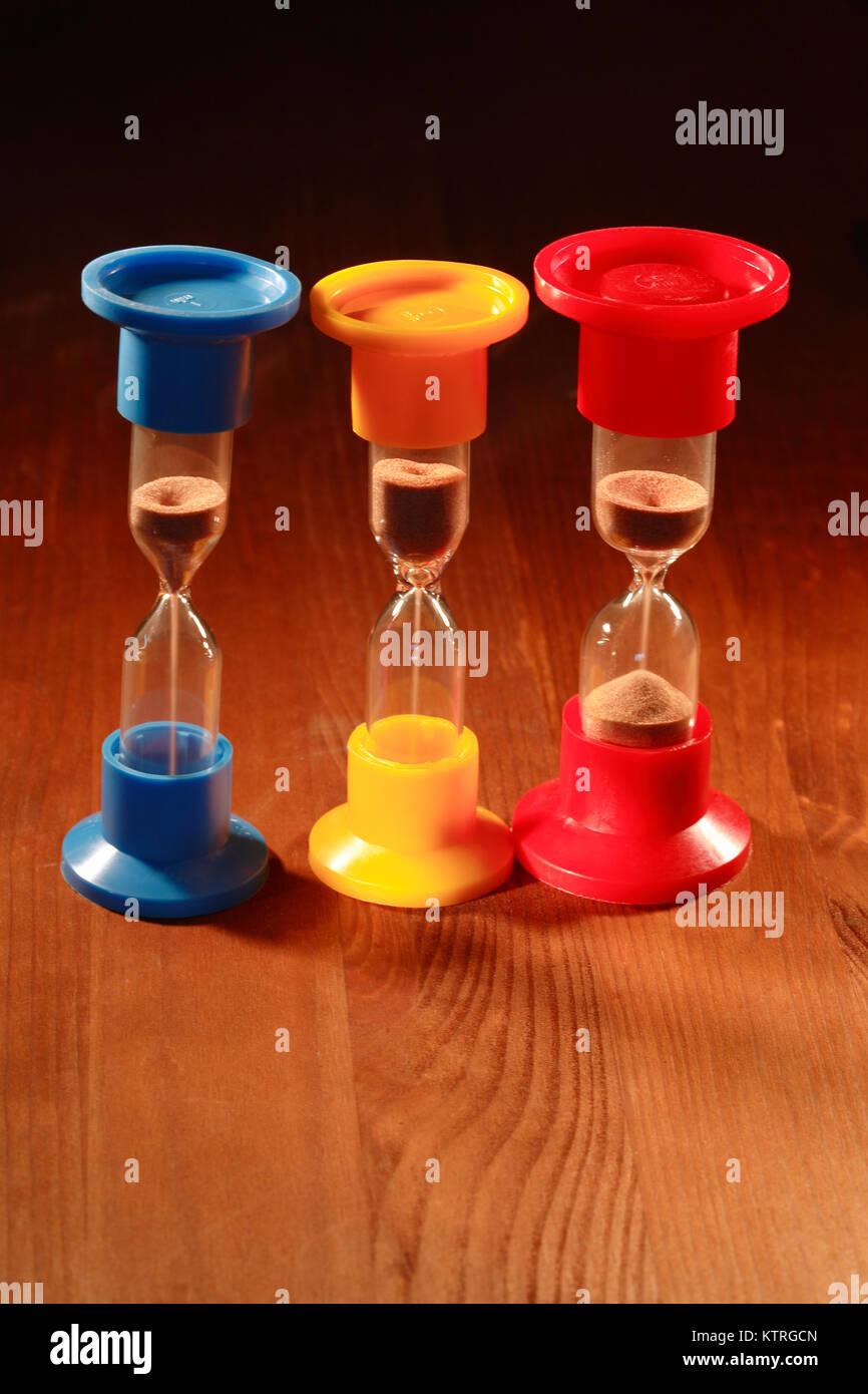 Three colored hourglasses standing on wooden background Stock Photo - Alamy