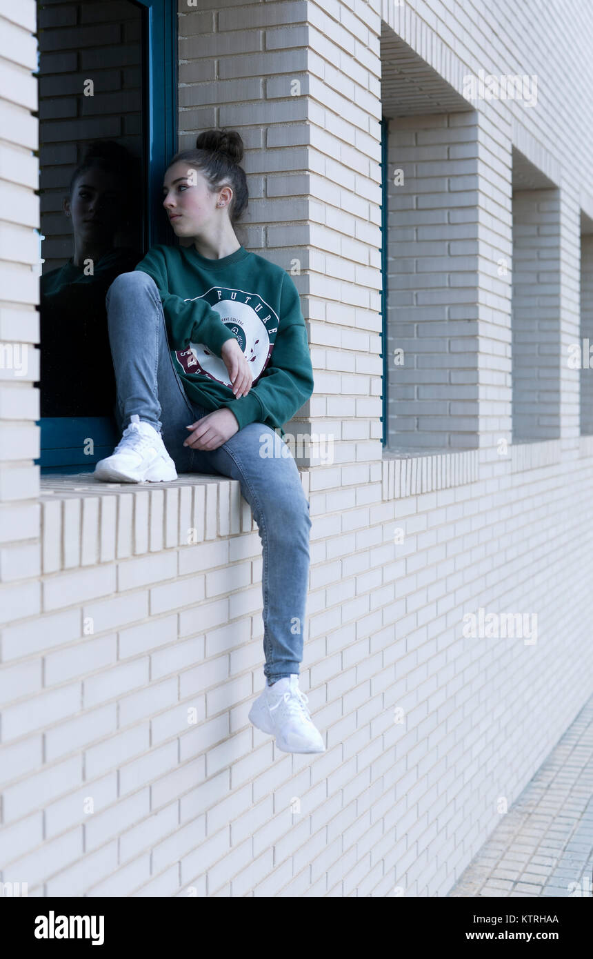 Teen girl sitting in the window of a building. Vertical shot with ...