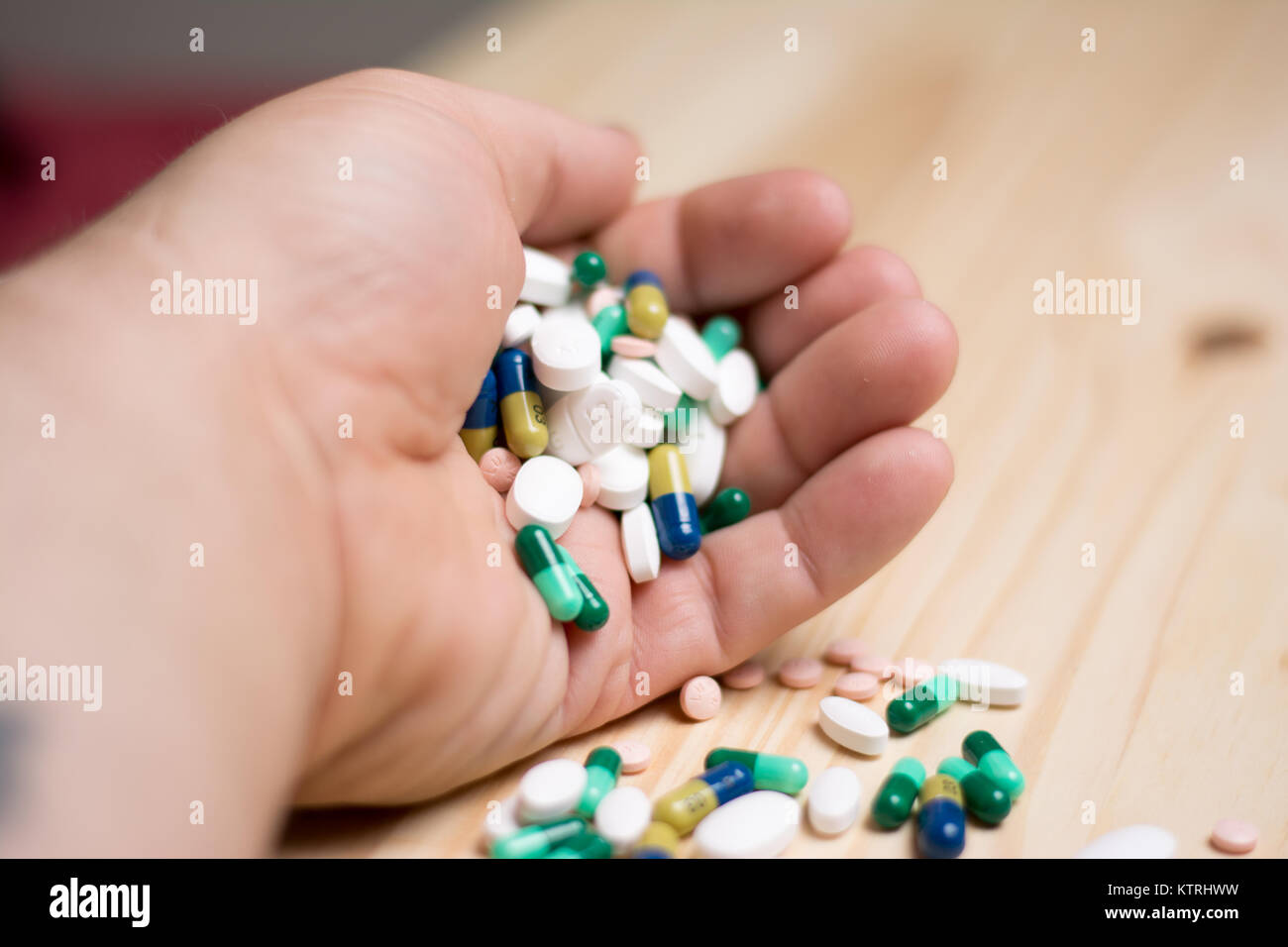 handful of different colored pills being held over wood background ...