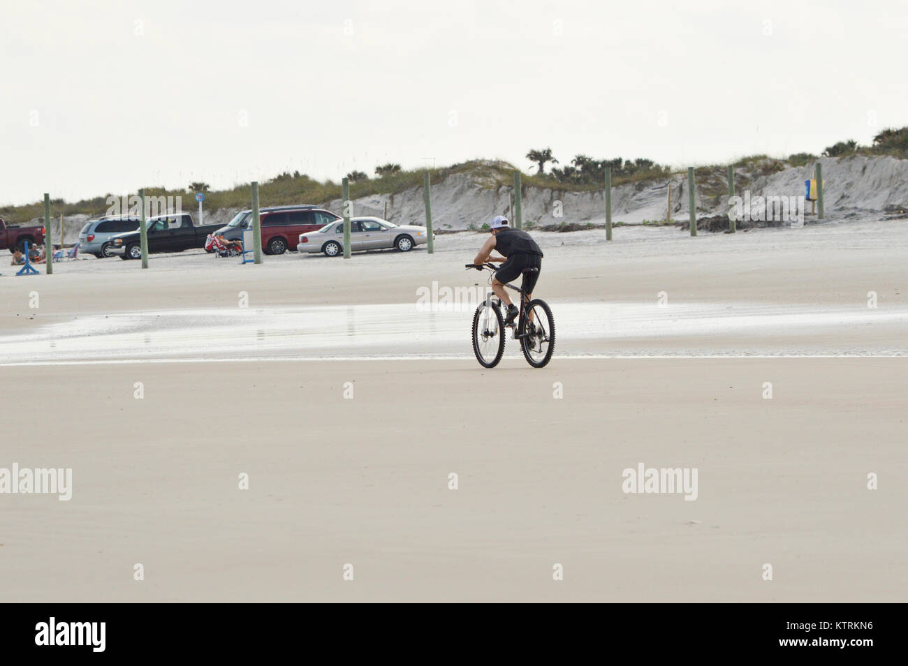A guy biking as fast as he can down the beach on a clear and sunny day ...