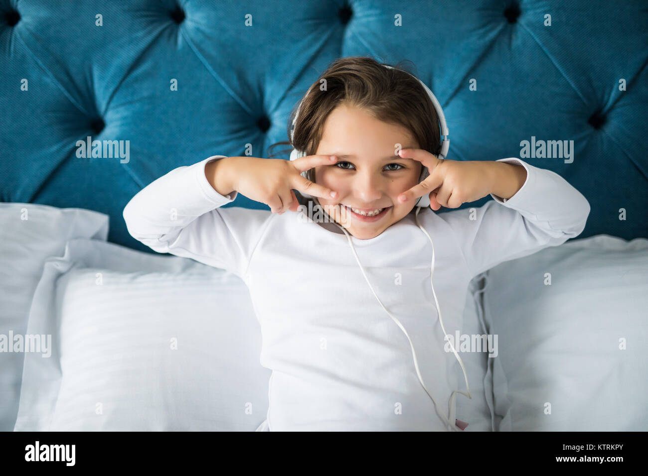 Cheerful girl listening to music and dancing while sitting in her bed ...