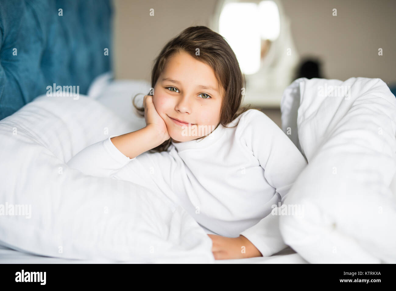 Close-up portrait of beautiful little kid lying on bed with hand under ...
