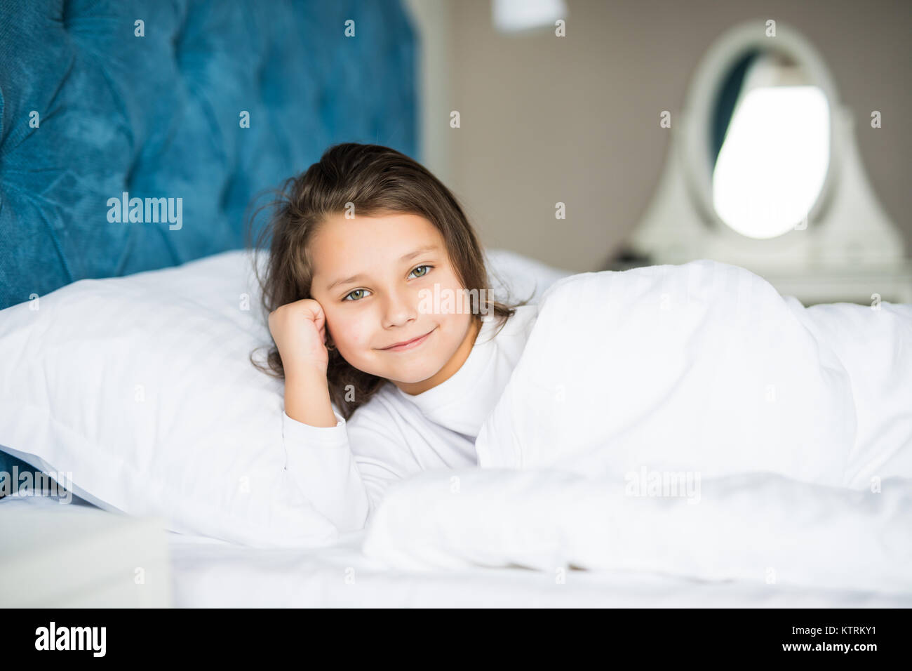 Close-up portrait of beautiful little kid lying on bed with hand under ...
