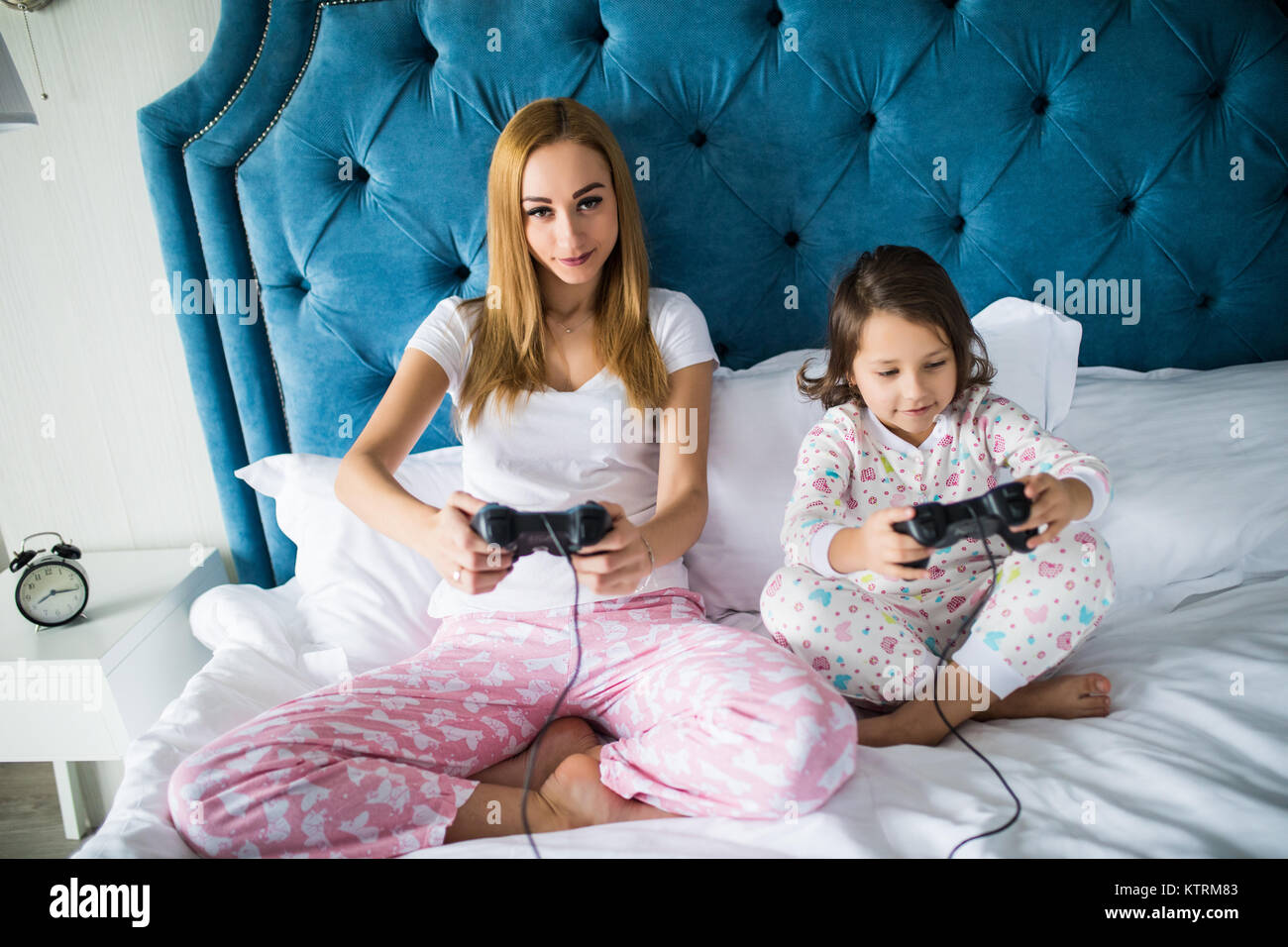 Mother and daughter plays game console video games on bed at home Stock ...