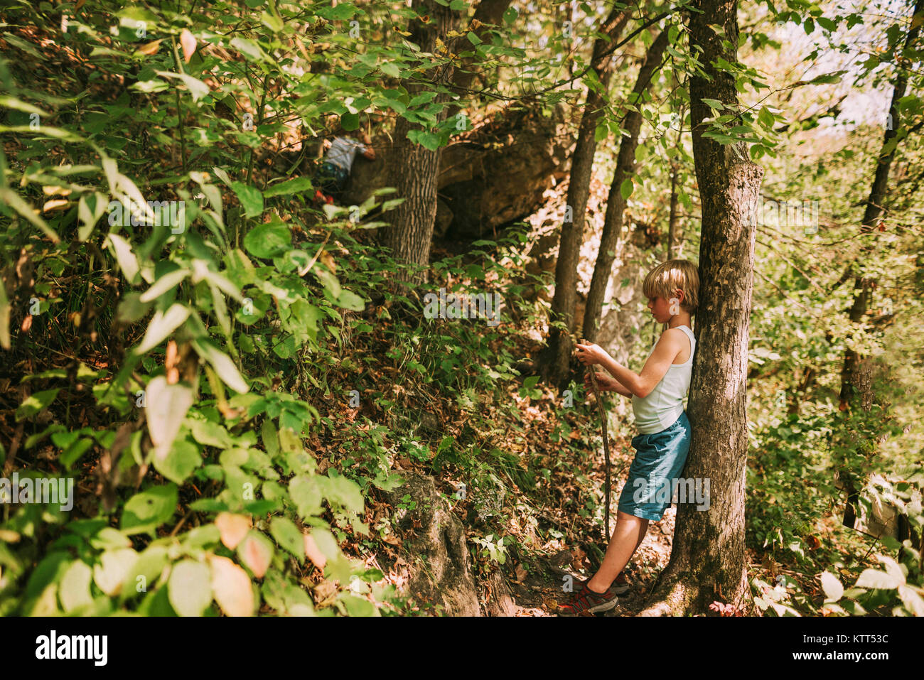 Boy leaning against a tree in the woods Stock Photo - Alamy