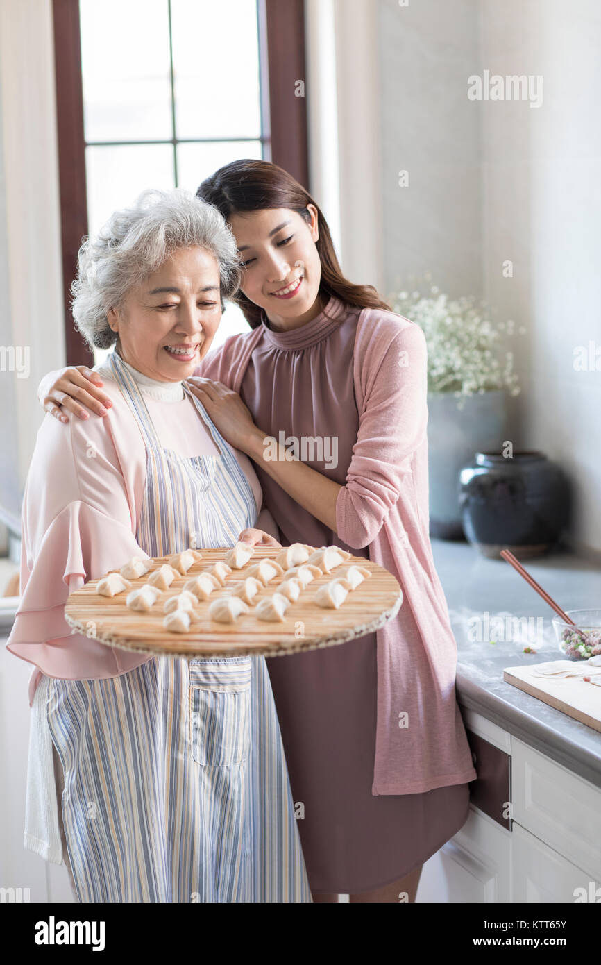 Cheerful mother and daughter making dumplings in kitchen Stock Photo ...