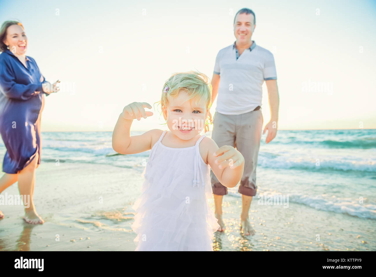 Laughing Baby girl running forward with smiling parents on the ...
