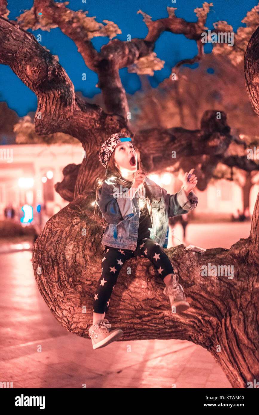 preschool girl sitting on a tree branch Stock Photo - Alamy