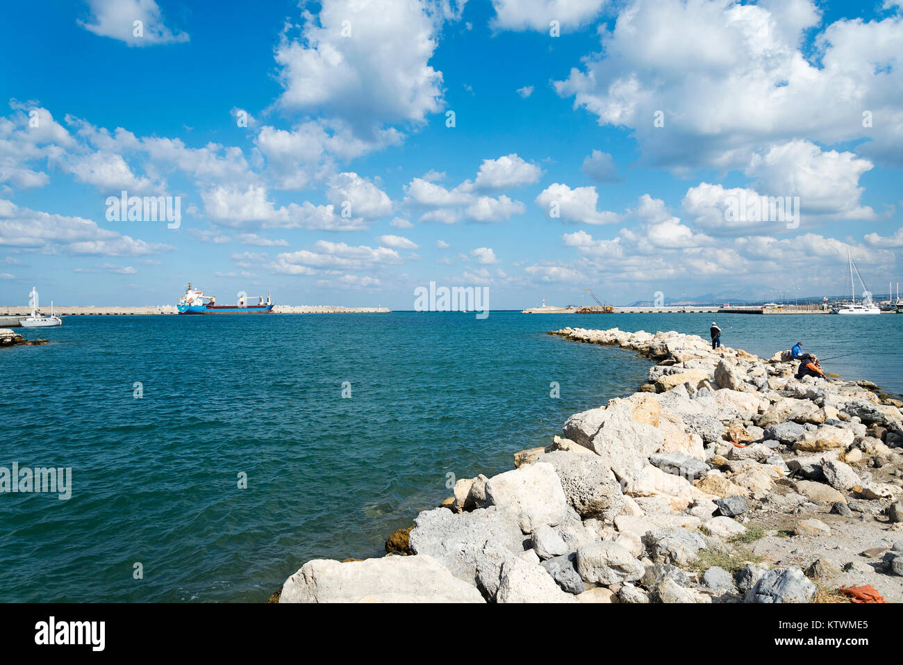 A fisherman in a vest and hat fishing on the rocks in the sea waves ...