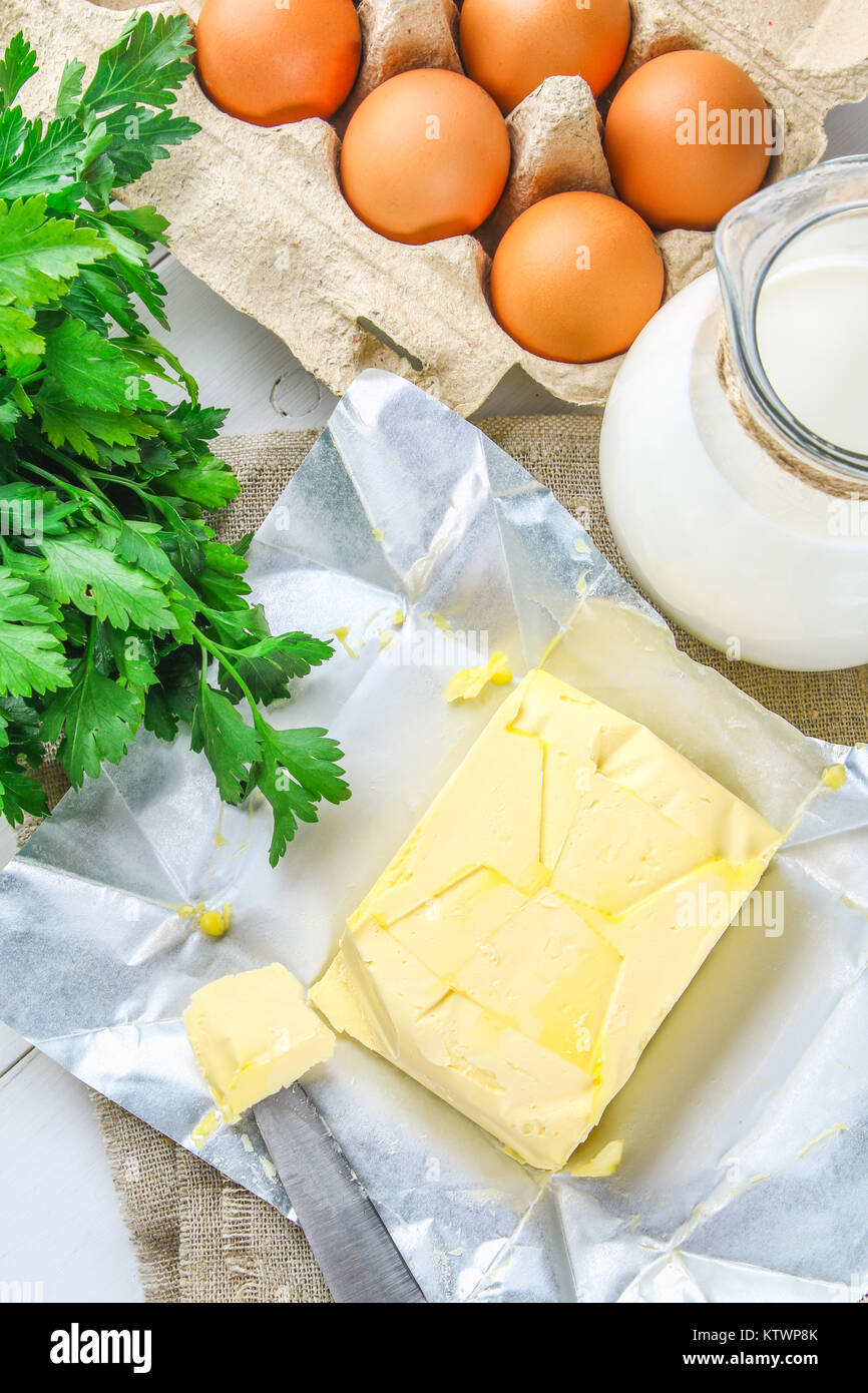 A bar of butter is cut into pieces on a wooden board with a knife ...