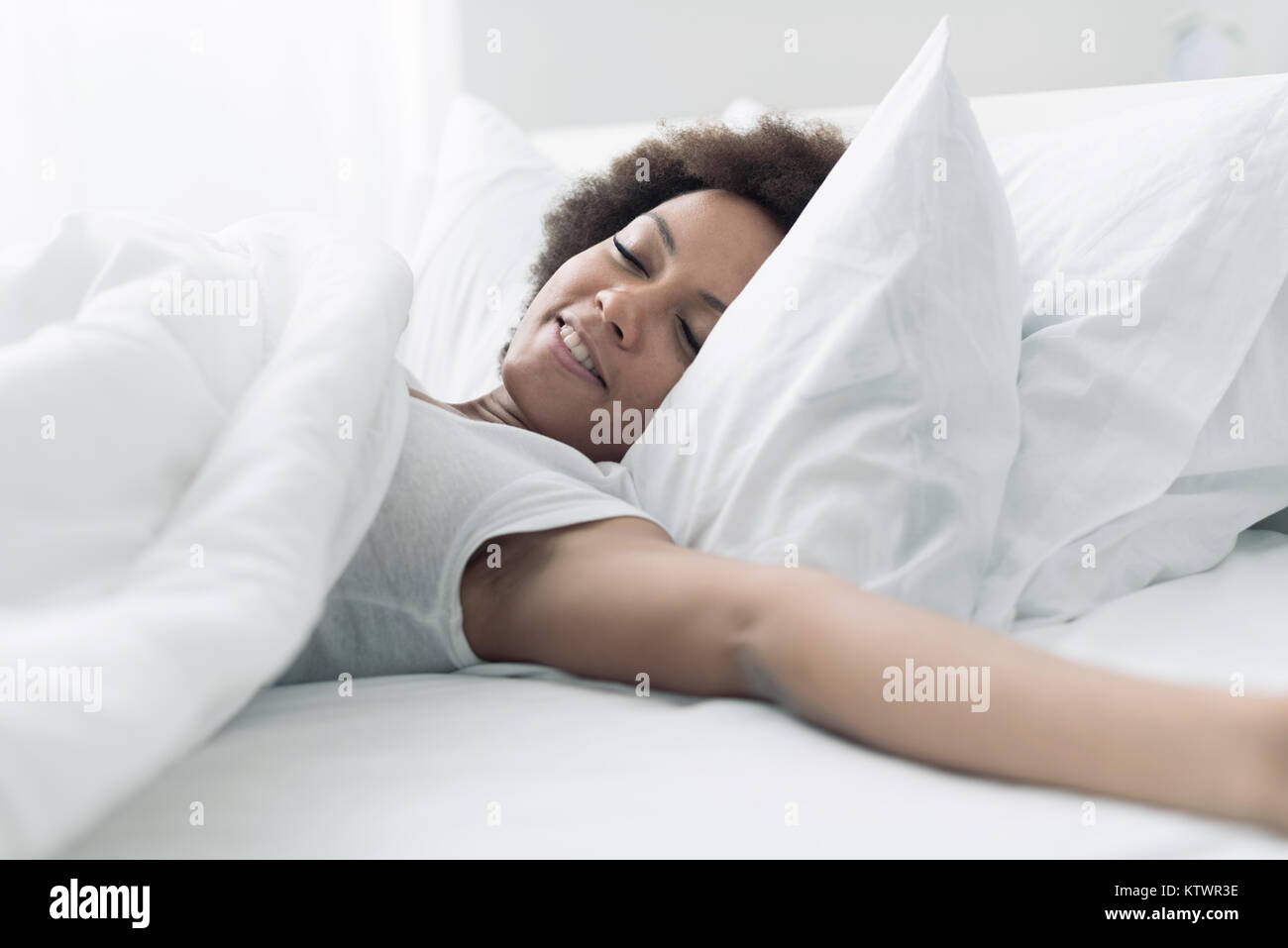 Beautiful woman waking up in her bed, she is smiling and stretching ...