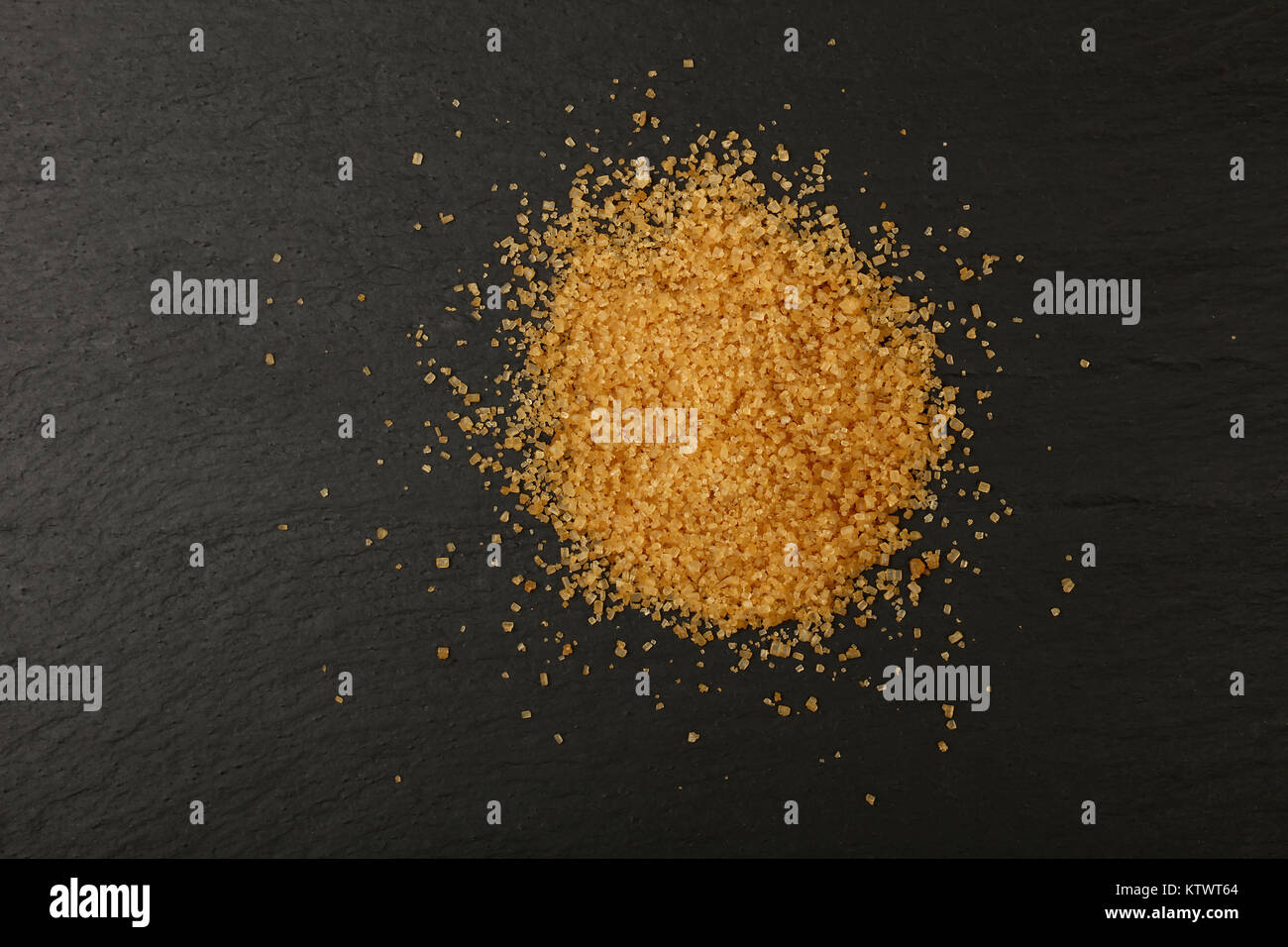 Close up pinch of brown cane sugar spilled on black slate board ...
