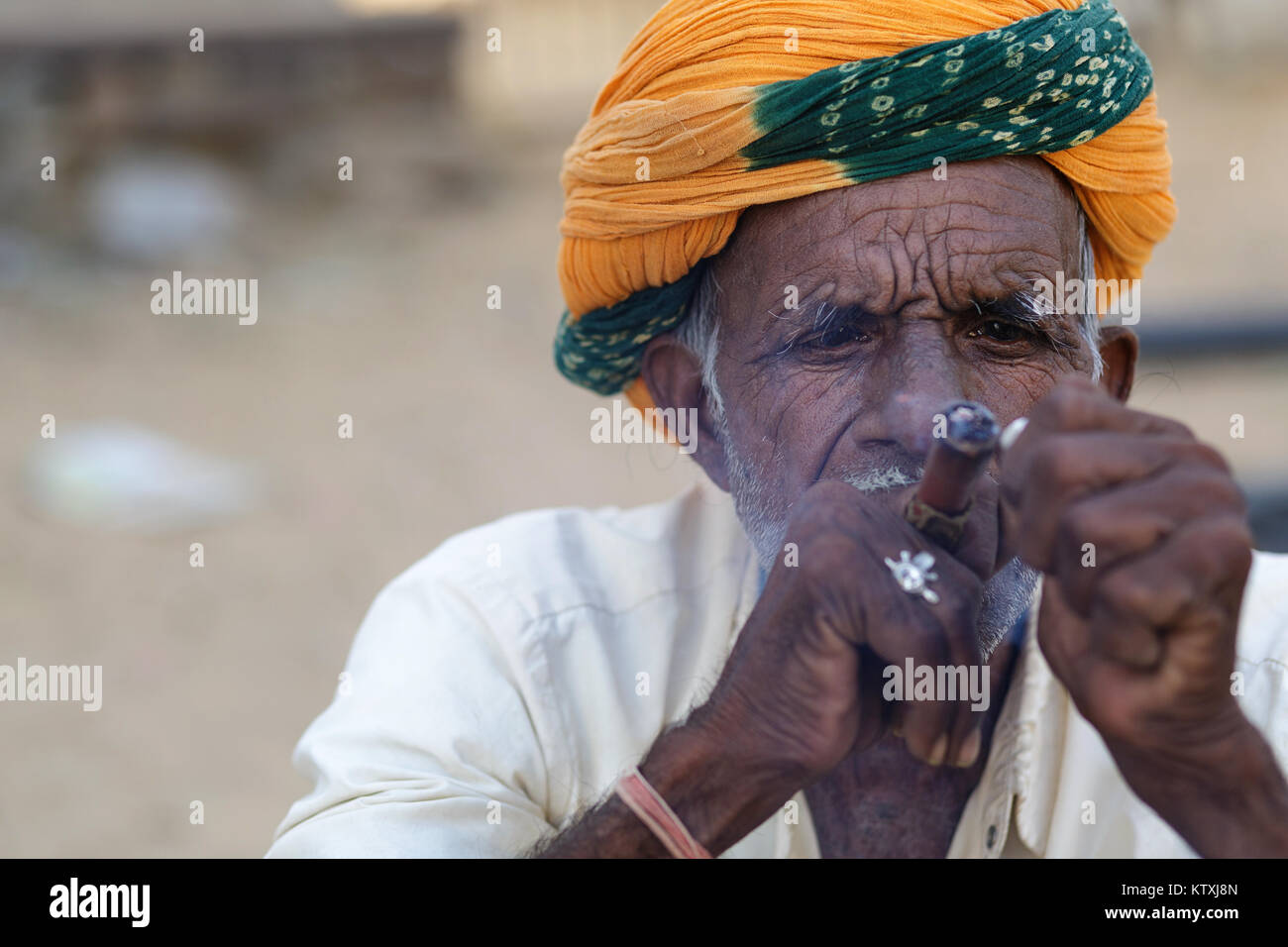 Indian man wearing yellow turban smoking a traditional cigar, village ...