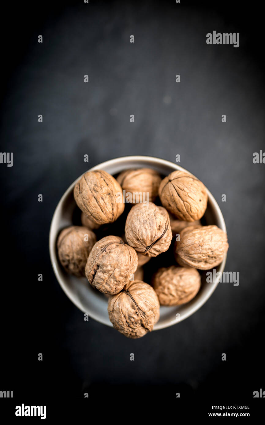 A bowl of whole walnuts in their shells in a bowl shot from above on a ...