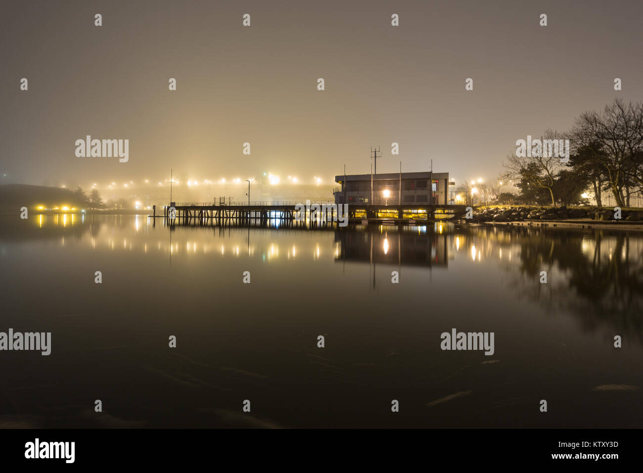 Dock by the ocean with a bridge illuminated on a foggy night Stock ...