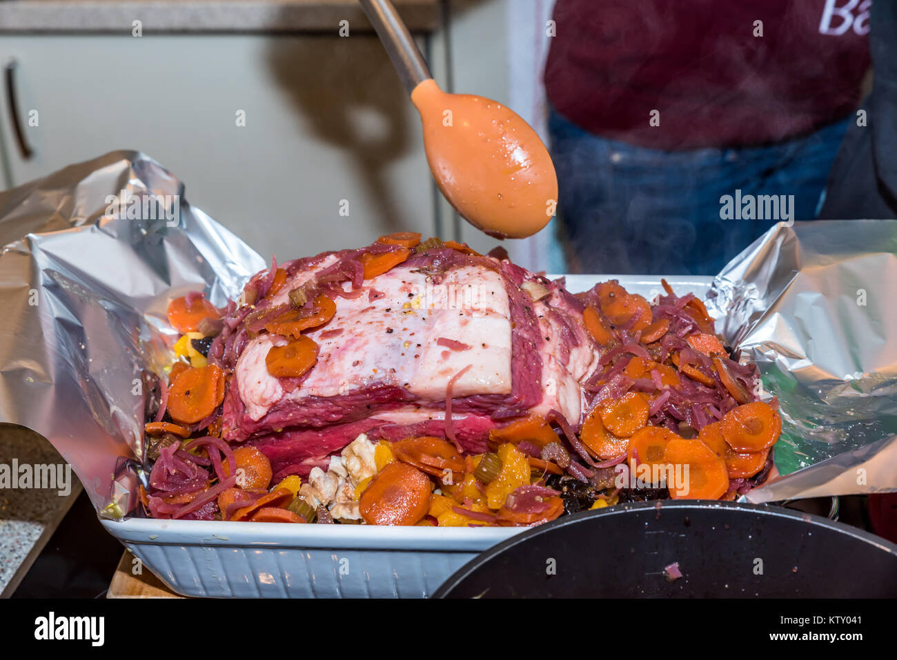 Male hand spraying cooked vegetables with sauce over raw beef rib steak ...