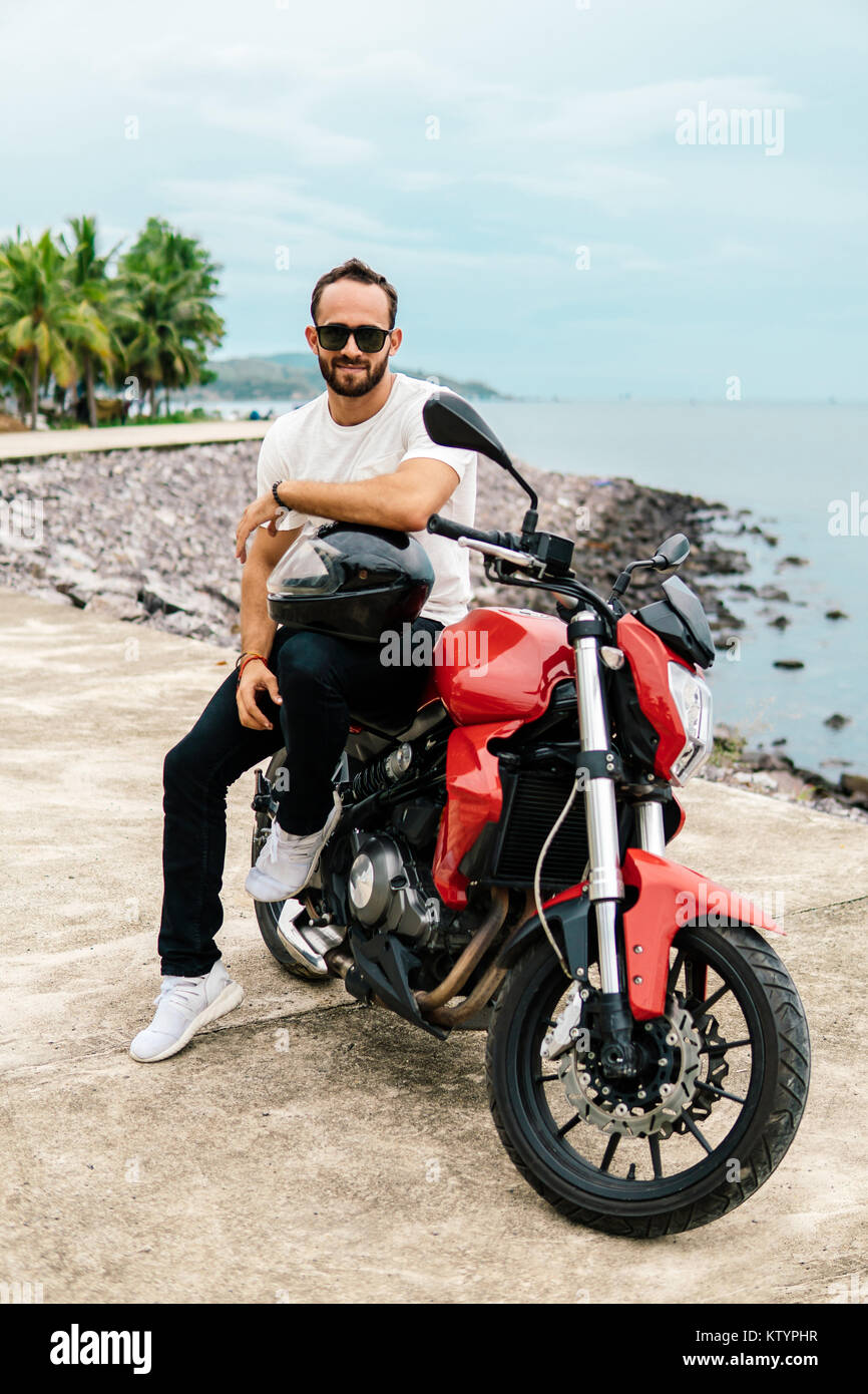Man sitting on his motorbike, holding helmet on sea background Stock ...