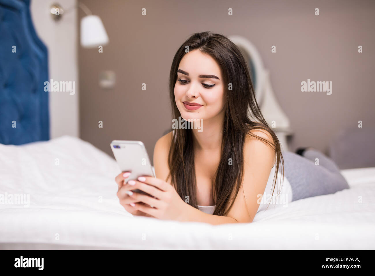 technology, communication and people concept - happy young woman lying in bed and texting on ...