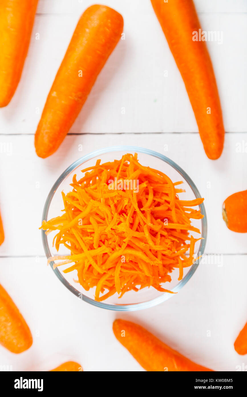 Grate carrots in a bowl on a white wooden table, top view. Tasty and ...