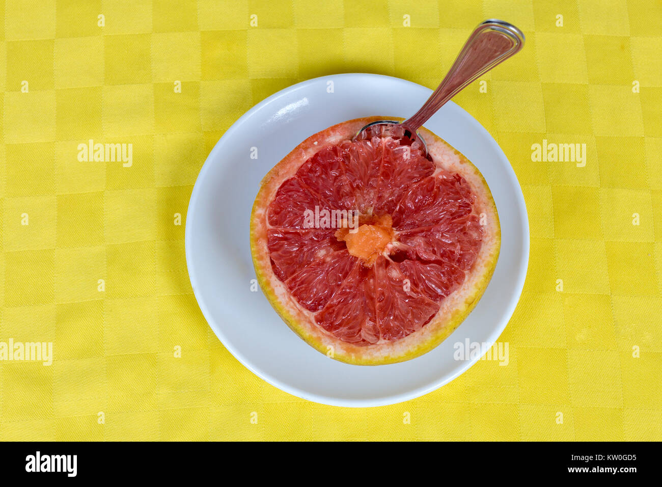 One half of a red grapefruit served in a white dish and a small spoon ...