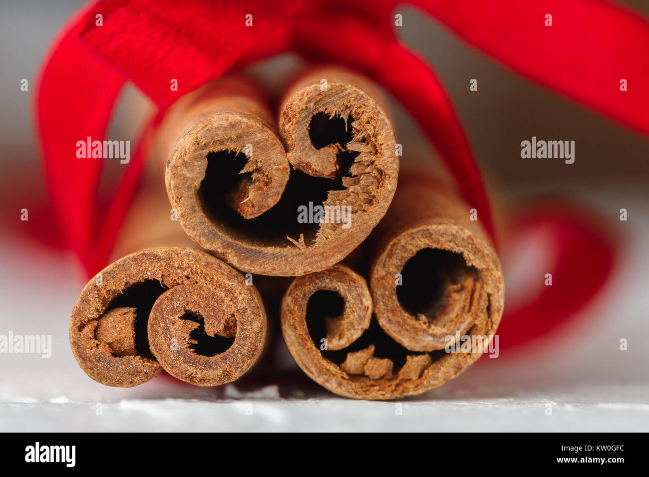 Festive wrapped cinnamon sticks with red ribbon on white textured ...