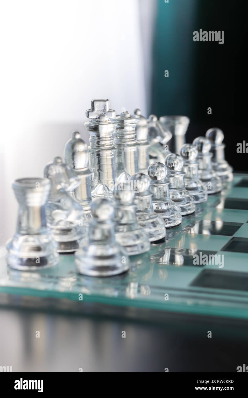 A clear glass chess set is set up and ready to play. The background is ...