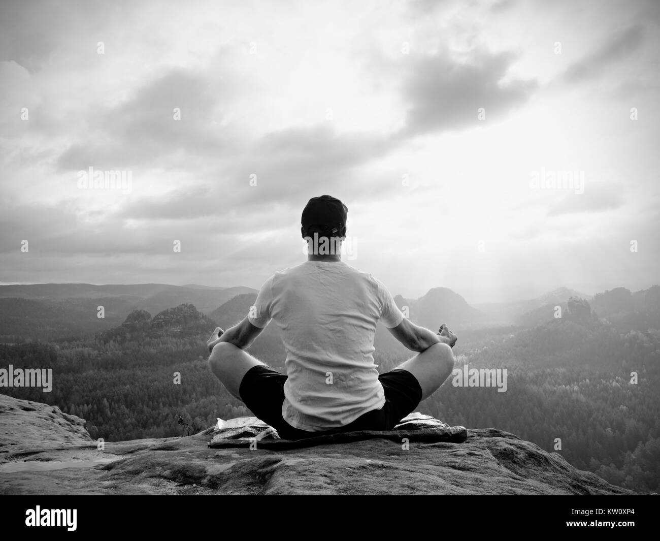 Alone sitting man practicing Yoga pose on the rocky peak. Man within ...