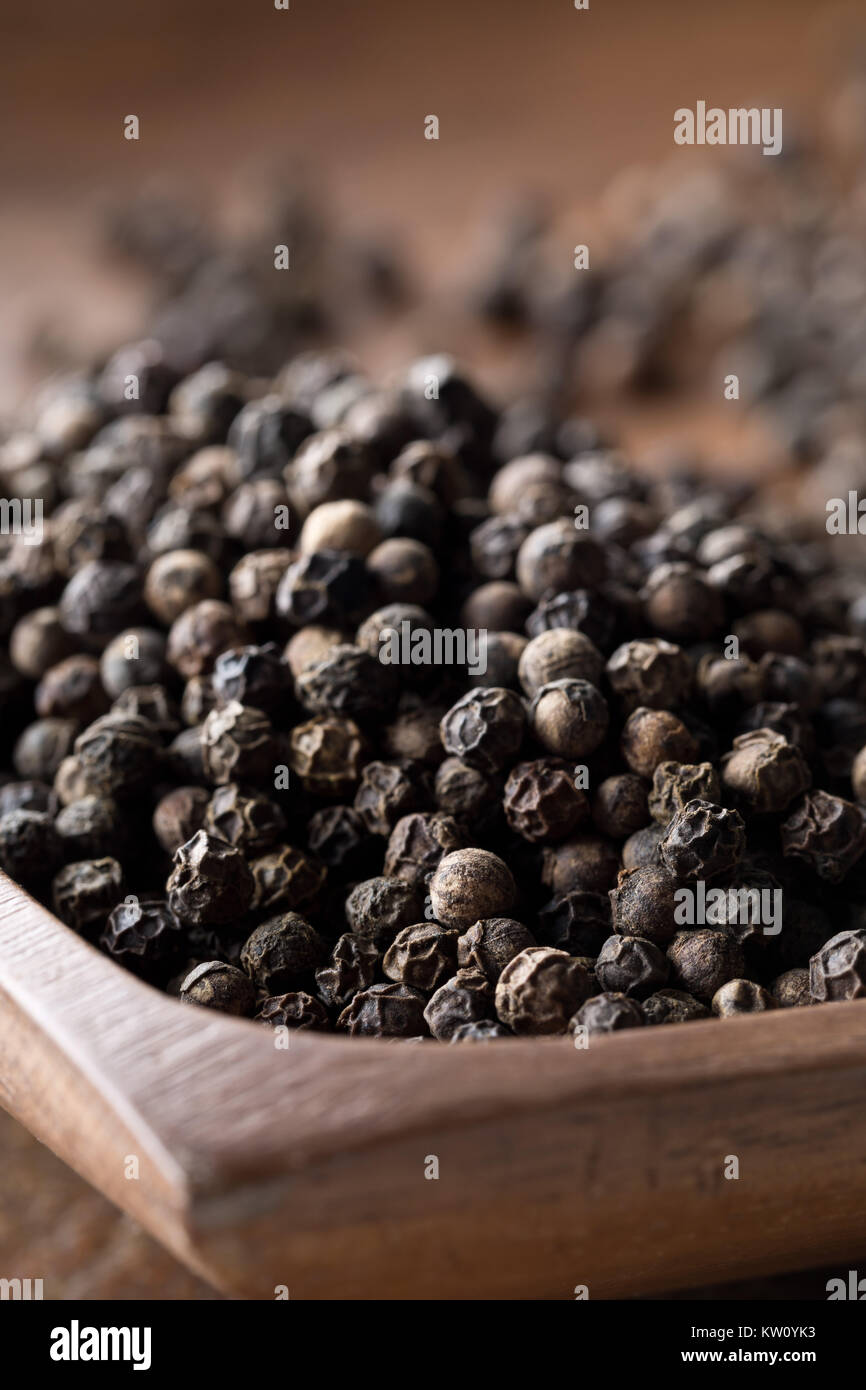 Raw, natural, unprocessed black pepper peppercorns on wooden plate with ...