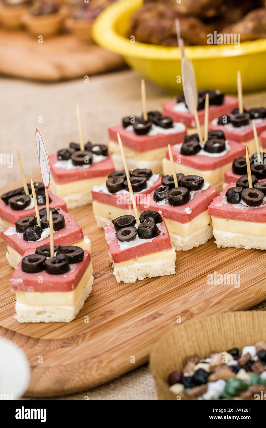 Canapes with sliced black olives, white cheese and salami on a wooden ...