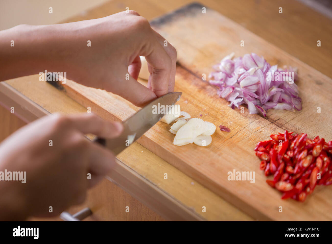 Hands slicing onion, garlic, and chilli on wooden cutting board Stock ...