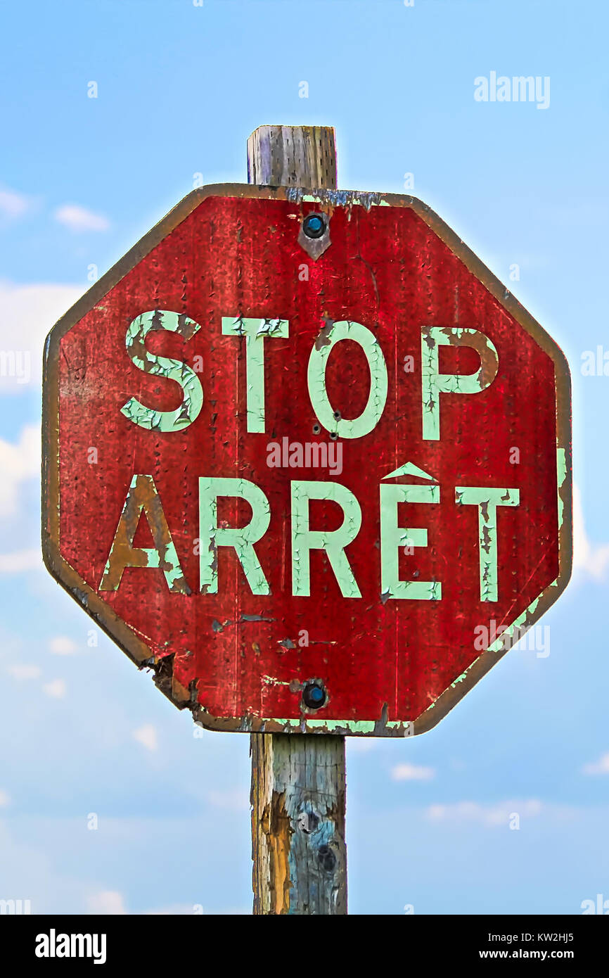 An old stop sign in both french and english against a blue sky Stock ...