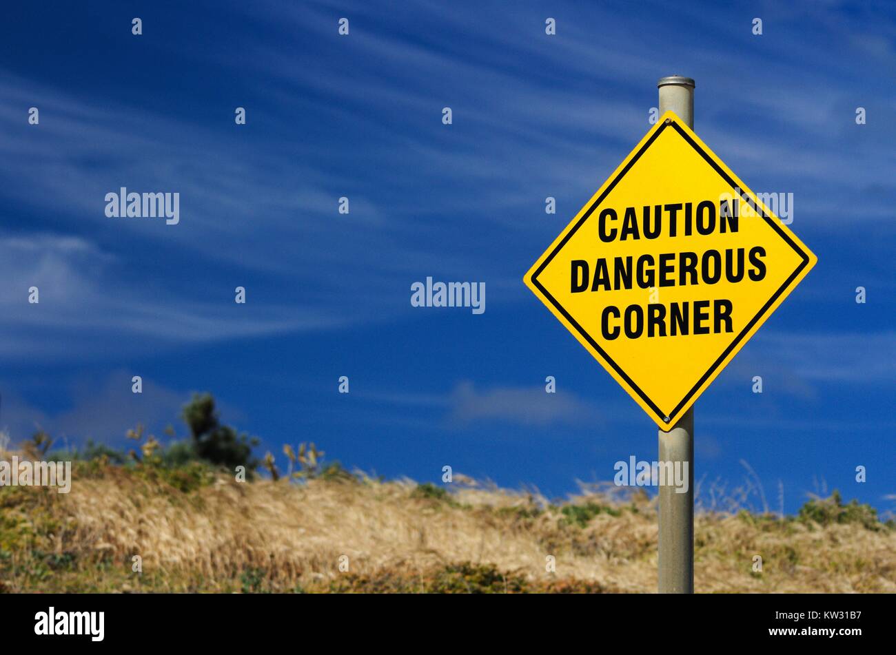 Yellow sign warning of dangerous corner against bright blue summer sky ...