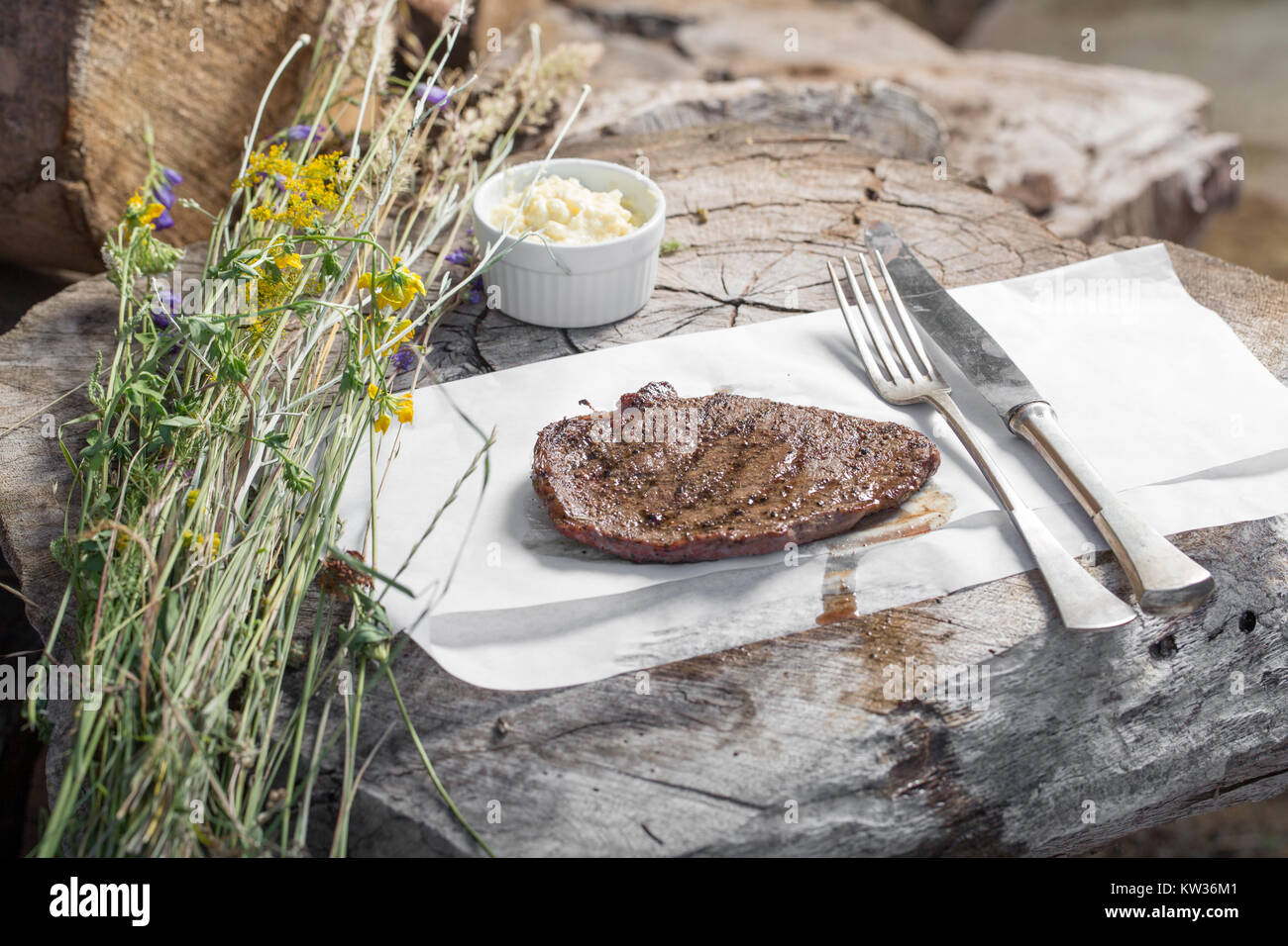 Beef steak on a rustic wooden log, with garlic sauce and old cutlery ...