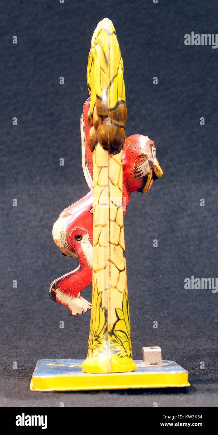 The image shows a tin toy monkey named Bombo, perched in a tree. It is ...