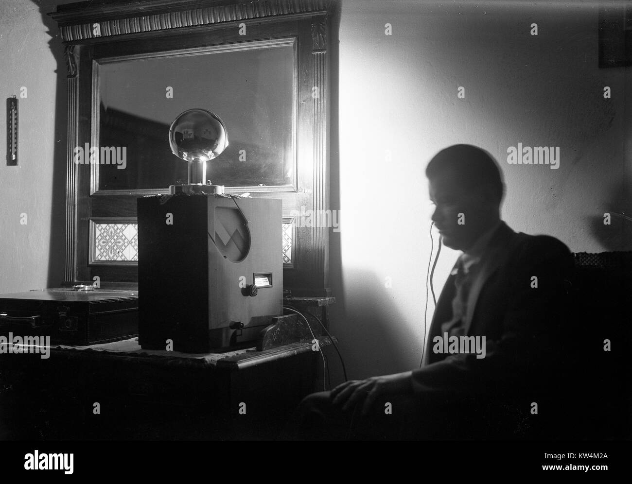 A man with a stern expression sits in a dark room and listens to a ...