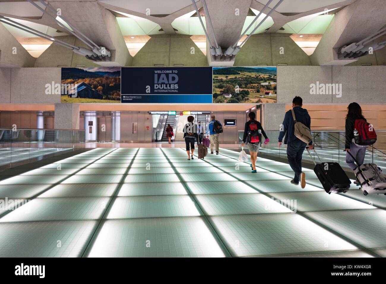 Passengers pull their rolling suitcases across a lighted glass bridge ...