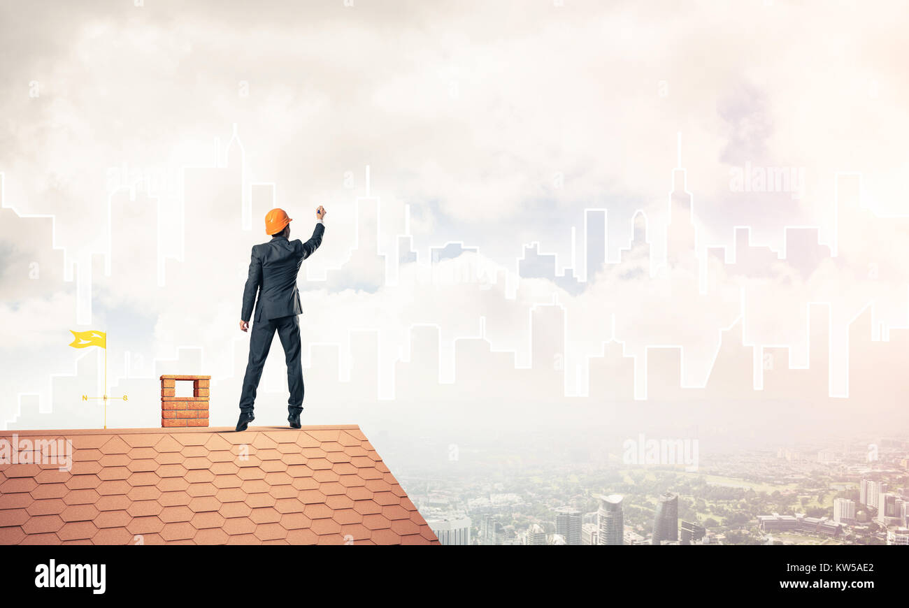Engineer man standing with back on house roof and drawing city. Mixed ...
