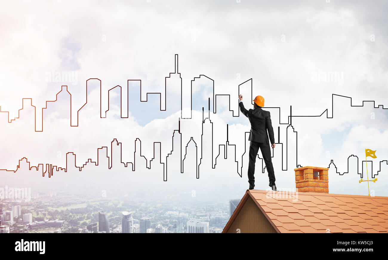 Engineer man standing with back on house roof and drawing city. Mixed ...