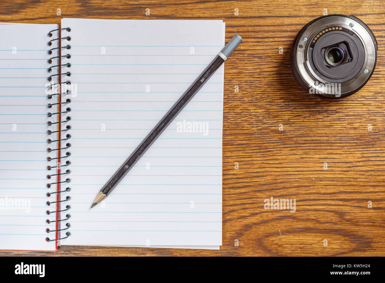Top view of open spiral notebook with black pencil and camera lens on ...