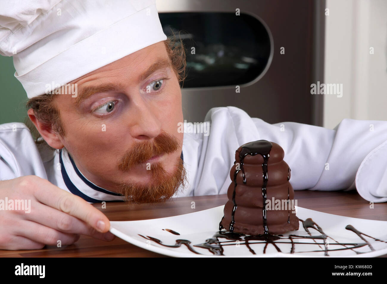 Funny young chef strange looking at piece of cake with chocolate sauce ...