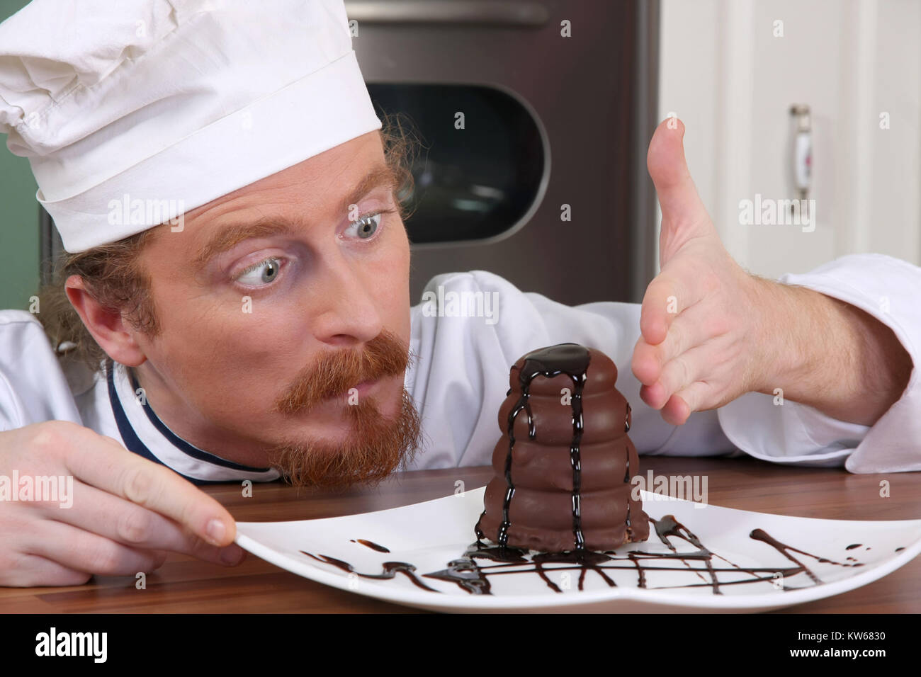 Funny young chef strange looking at piece of cake with chocolate sauce ...