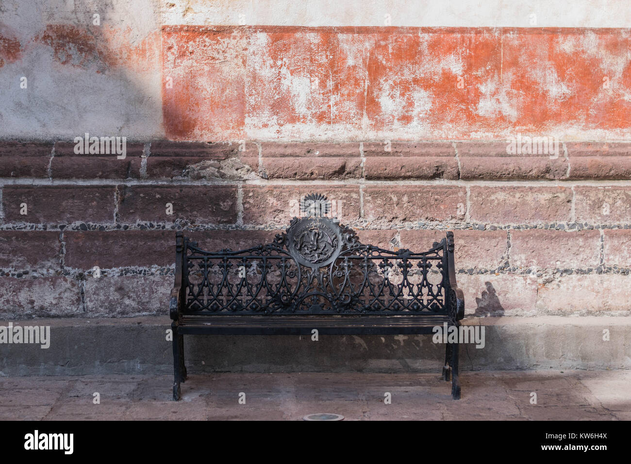 A decorative black iron bench, with a stone floor, a partial stone wall ...