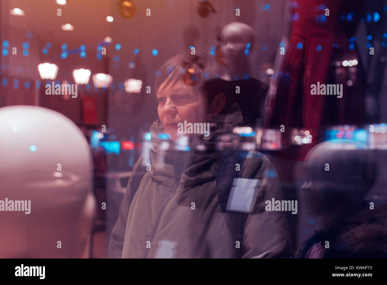 Thoughtful woman looking through shop window at night during the ...