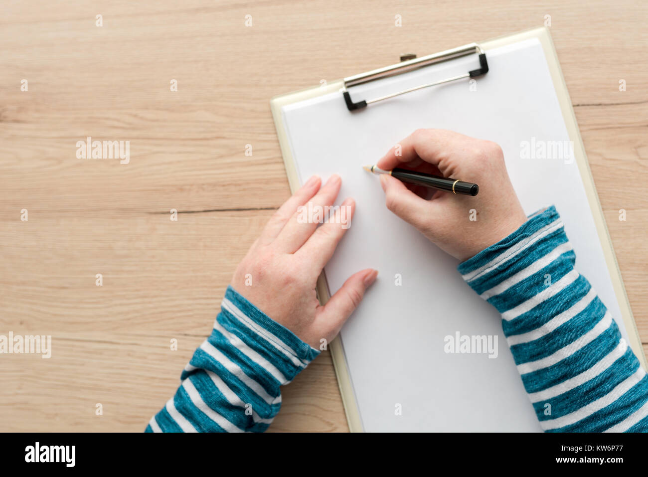 Woman writing on clipboard note pad paper, overhead view, selective ...